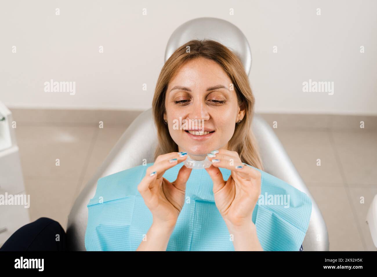 Smiling woman with healthy teeth holding removable clear braces aligner ...
