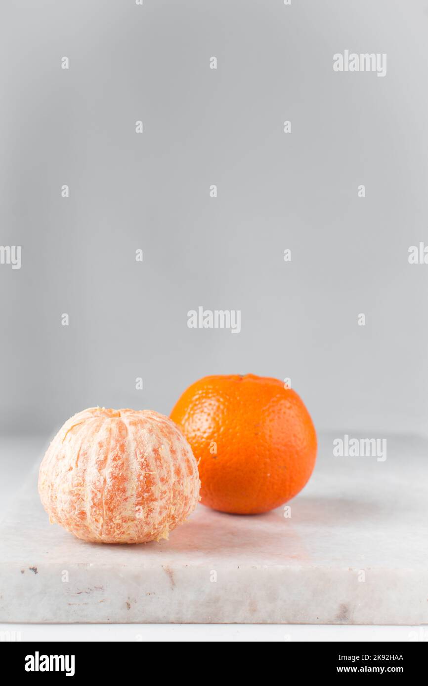 Peeled and unpeeled clementines on a marble chopping board, orange ...
