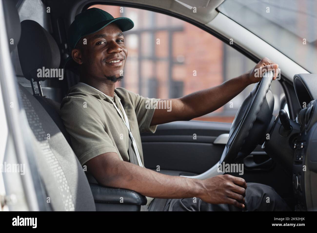 Side view portrait of smiling delivery man driving truck and looking at ...