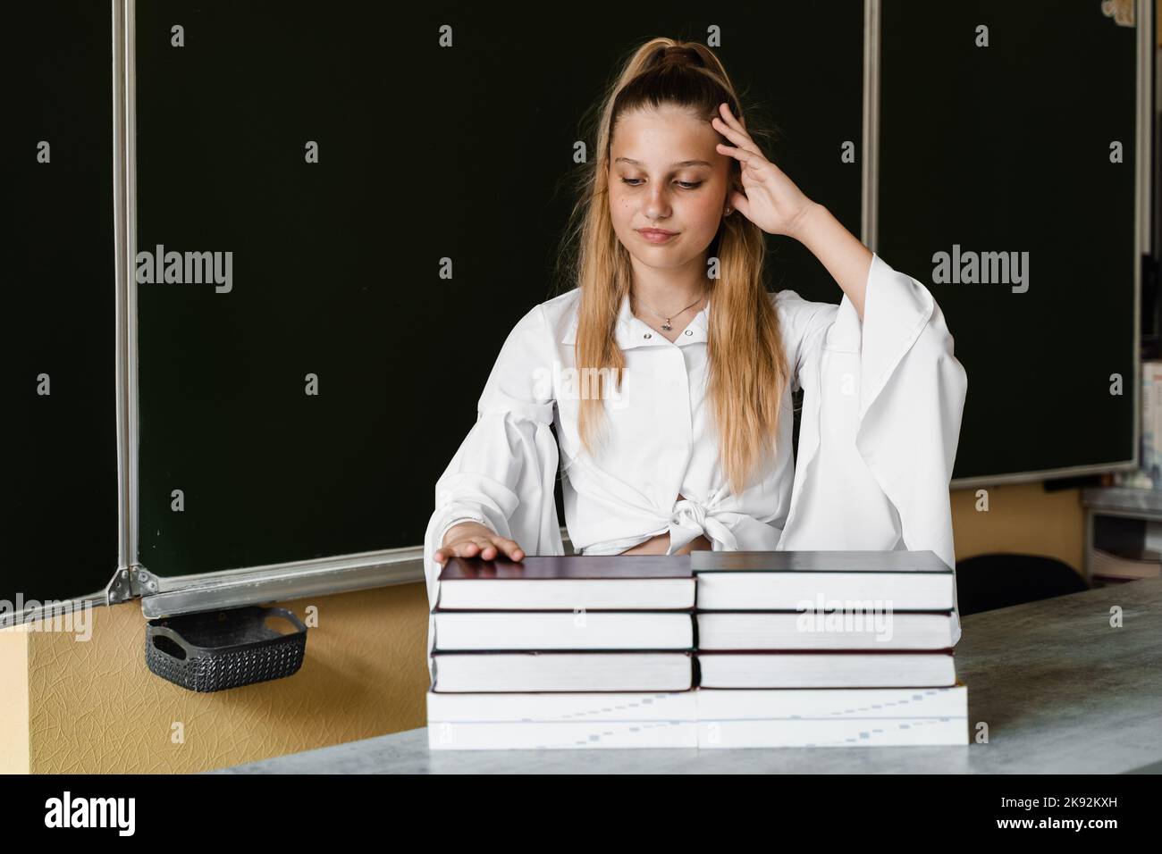 Tired and frustrated schoolgirl lies on books at blackboard in school ...