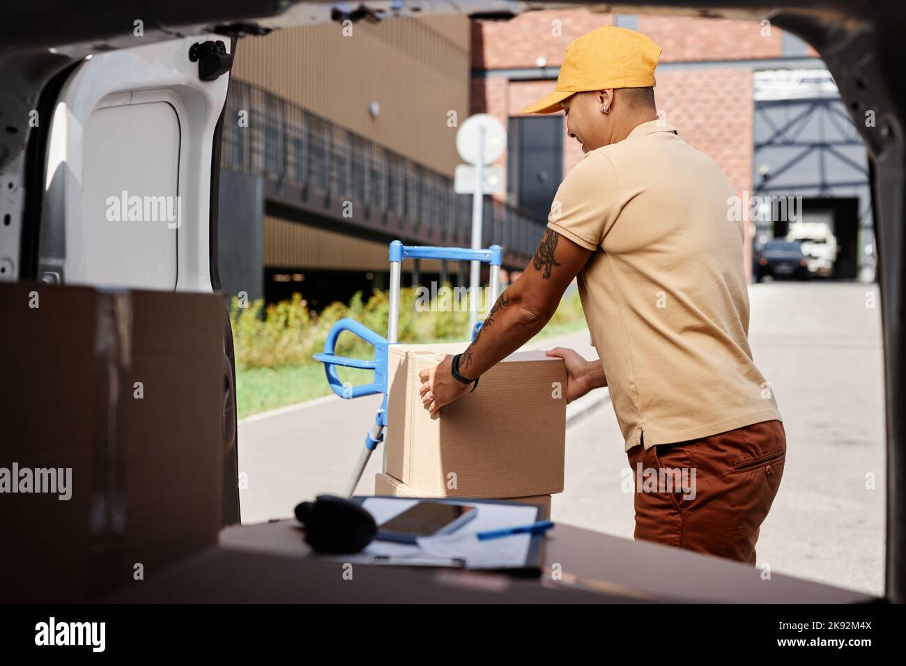 Back view of delivery worker holding box while unloading van trunk ...