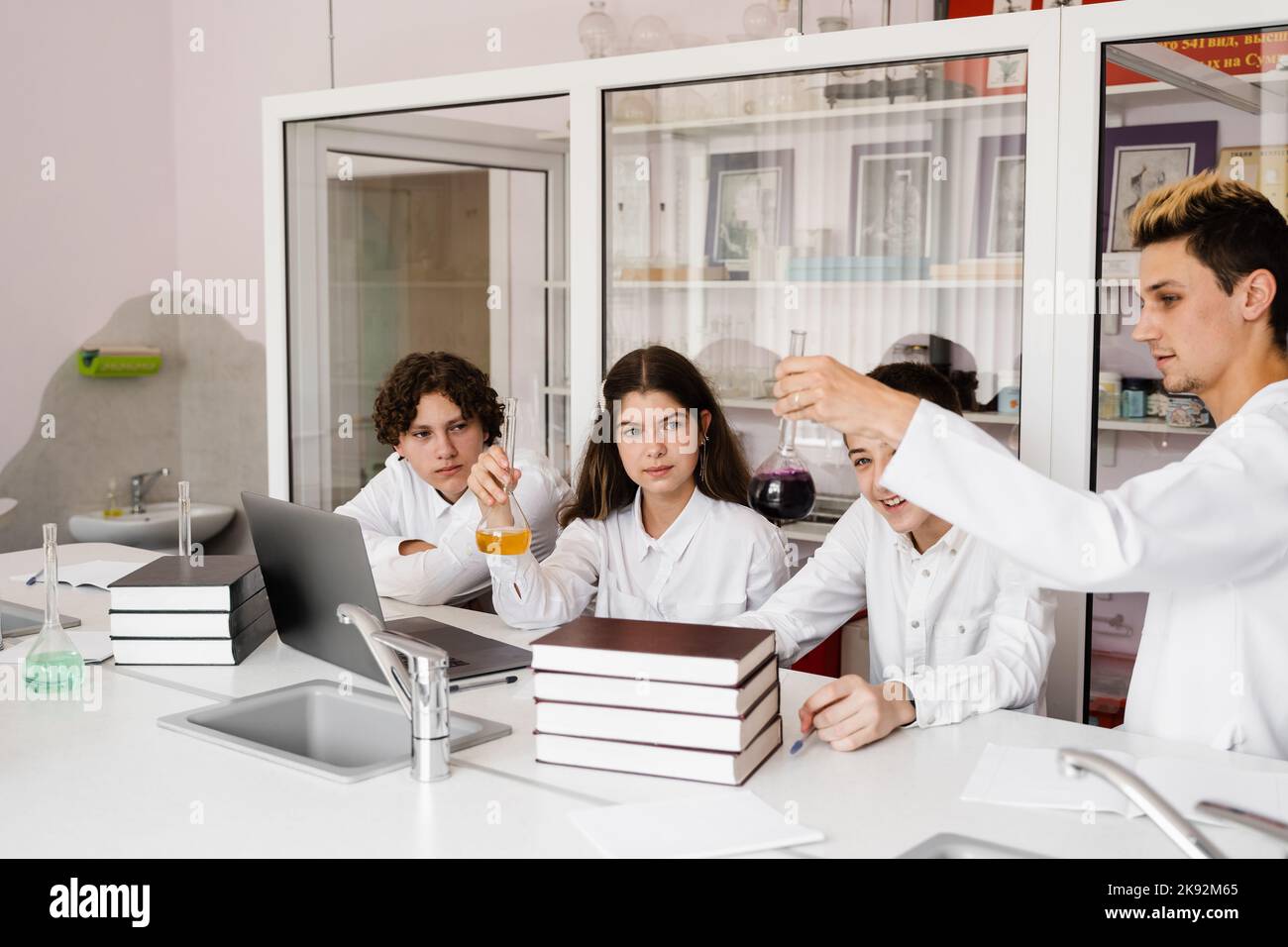 School teacher gives chemistry lesson to children in a laboratory with ...