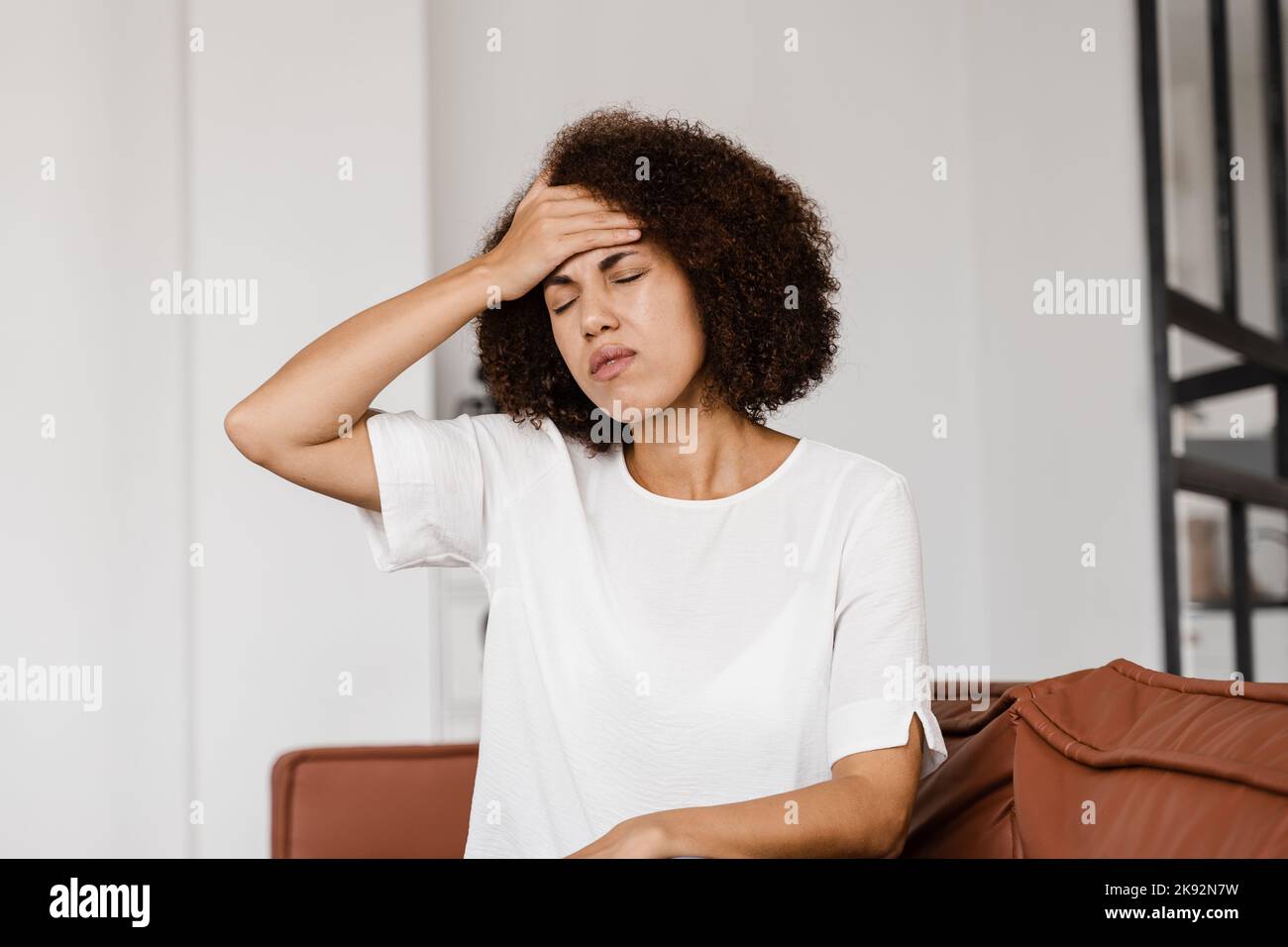 Sick African American woman has fever and touches her forehead with her ...