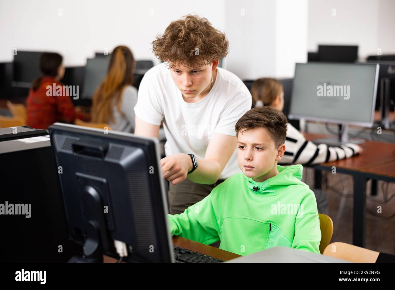 Teenager helps friend solve problem on computer in school class Stock ...