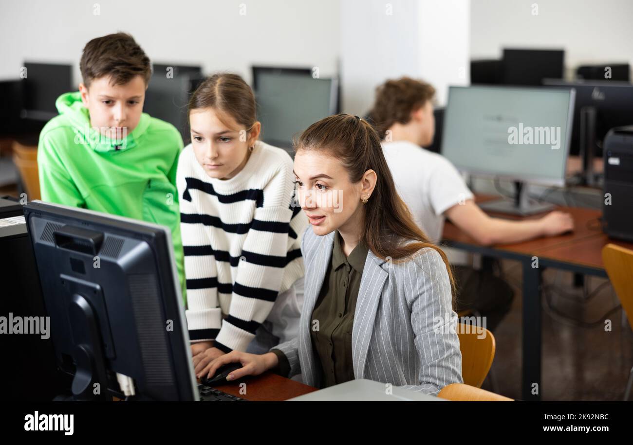 Teenagers studying with female teacher in information technology class ...