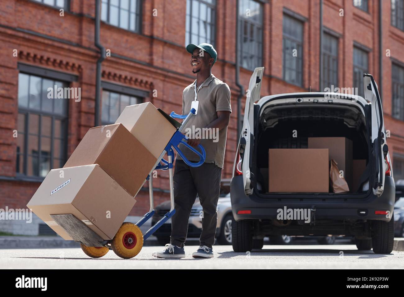 Full length portrait of smiling delivery worker unloading boxes ...
