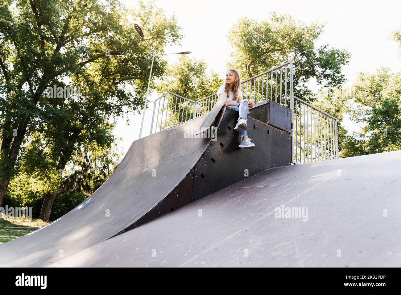 Child girl sitting with skate board on sport ramp. Sports equipment for ...