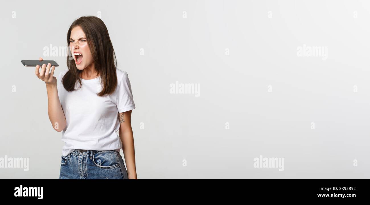 Angry brunette girl shouting mad while recording voice message, being ...