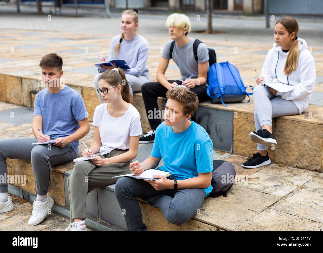 Students record lecture while sitting on a stone street parapet Stock Photo - Alamy