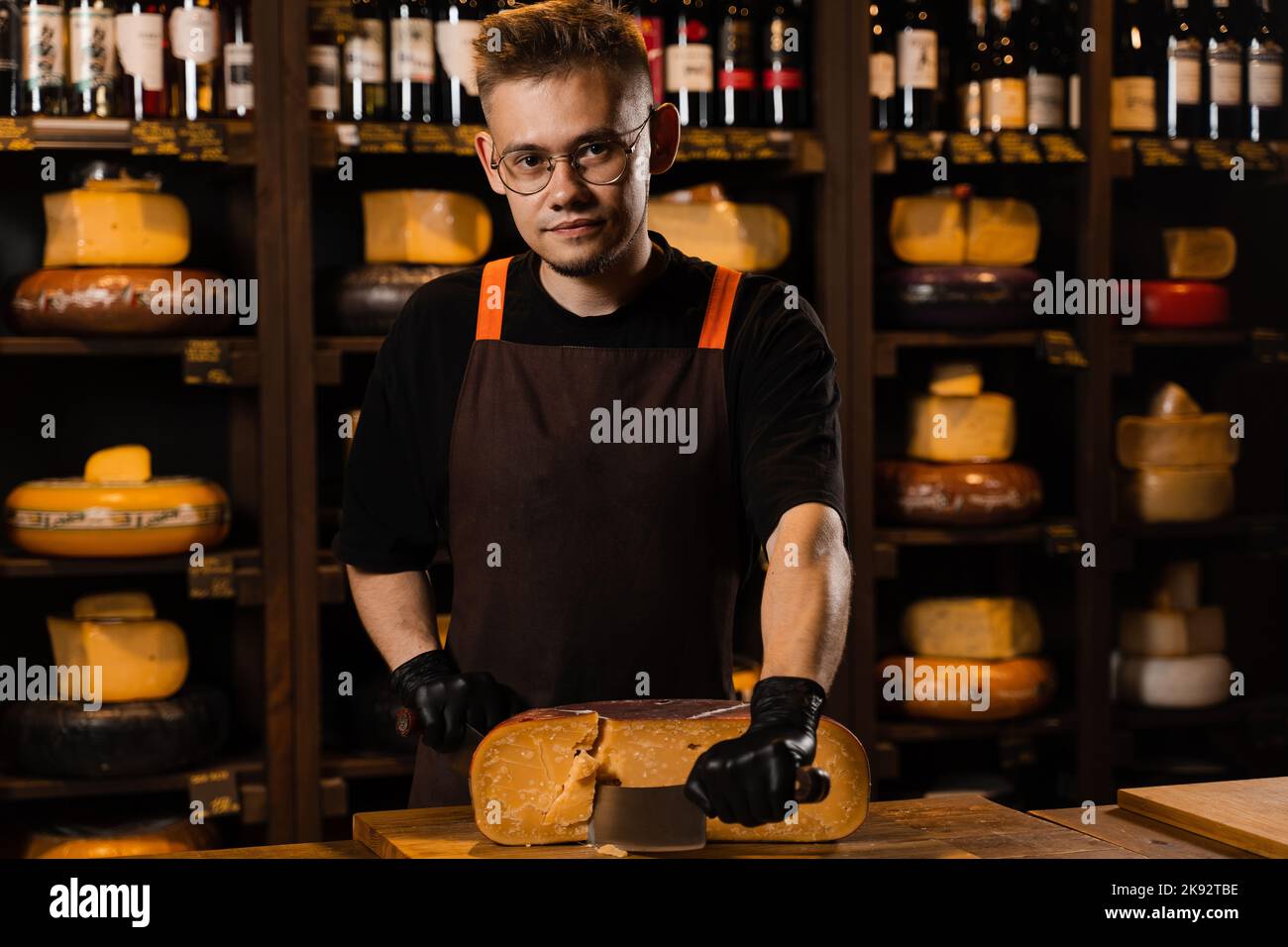 Handsome man worker of cheese shop cut limited gouda with knife. Cheese ...
