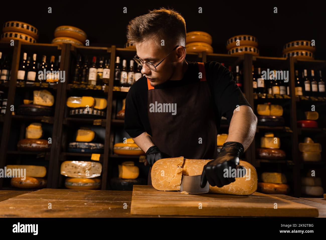 Handsome man worker of cheese shop cut limited gouda with knife. Cheese ...