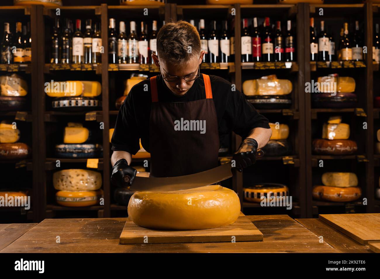 Cheese sommelier cutting yellow cheese wheel cut in half with a knife ...