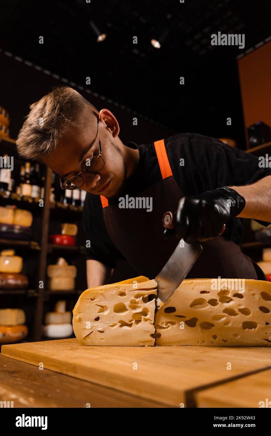 Cheese sommelier in food shop worker is cutting limited maasdam natural ...