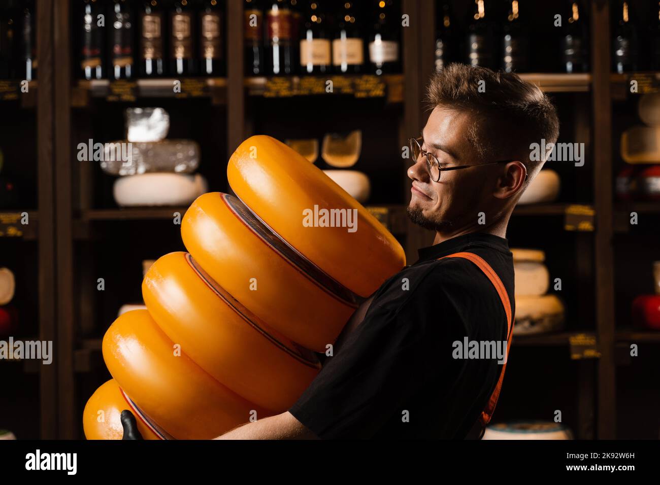 Handsome cheese sommelier with yellow wheels of cheese in shop. Worker ...