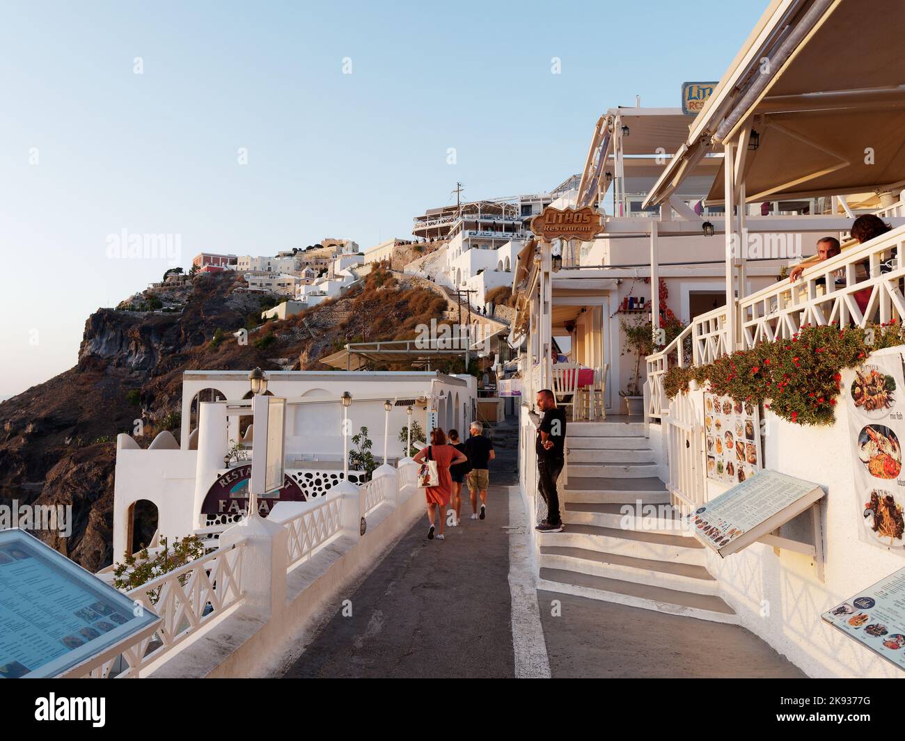 Street in Fira town in the evening with restaurants and tourists. Greek ...