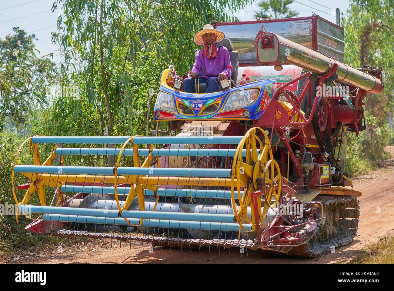 A man sits on a rice harvesting machine on a small rural road in ...