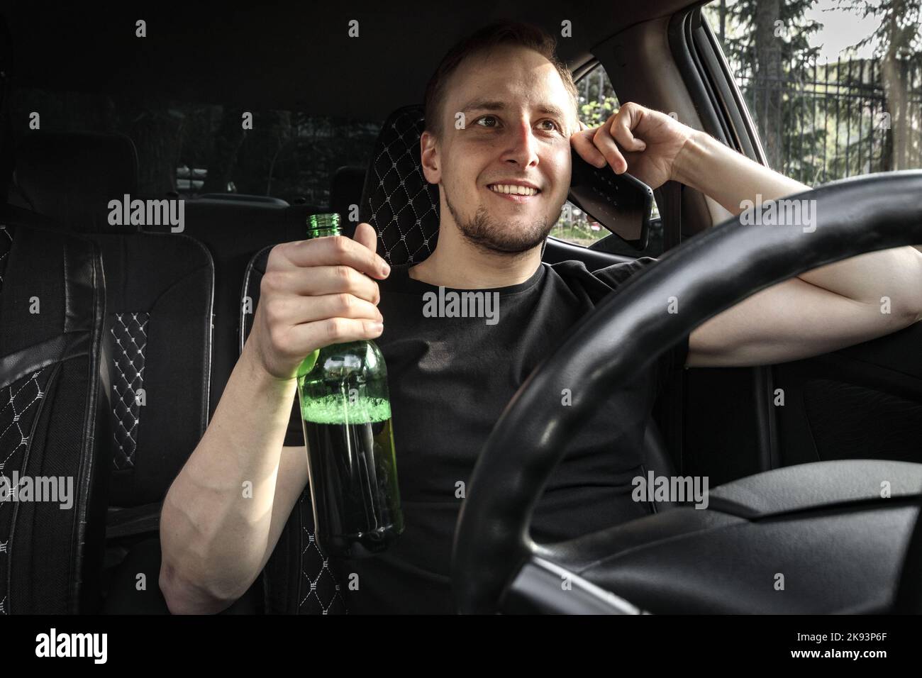 Drunk smiling driver with a bottle of beer driving a car talk on the ...