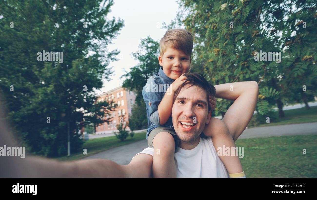 POV of Happy father carrying his smiling son on neck and making video ...
