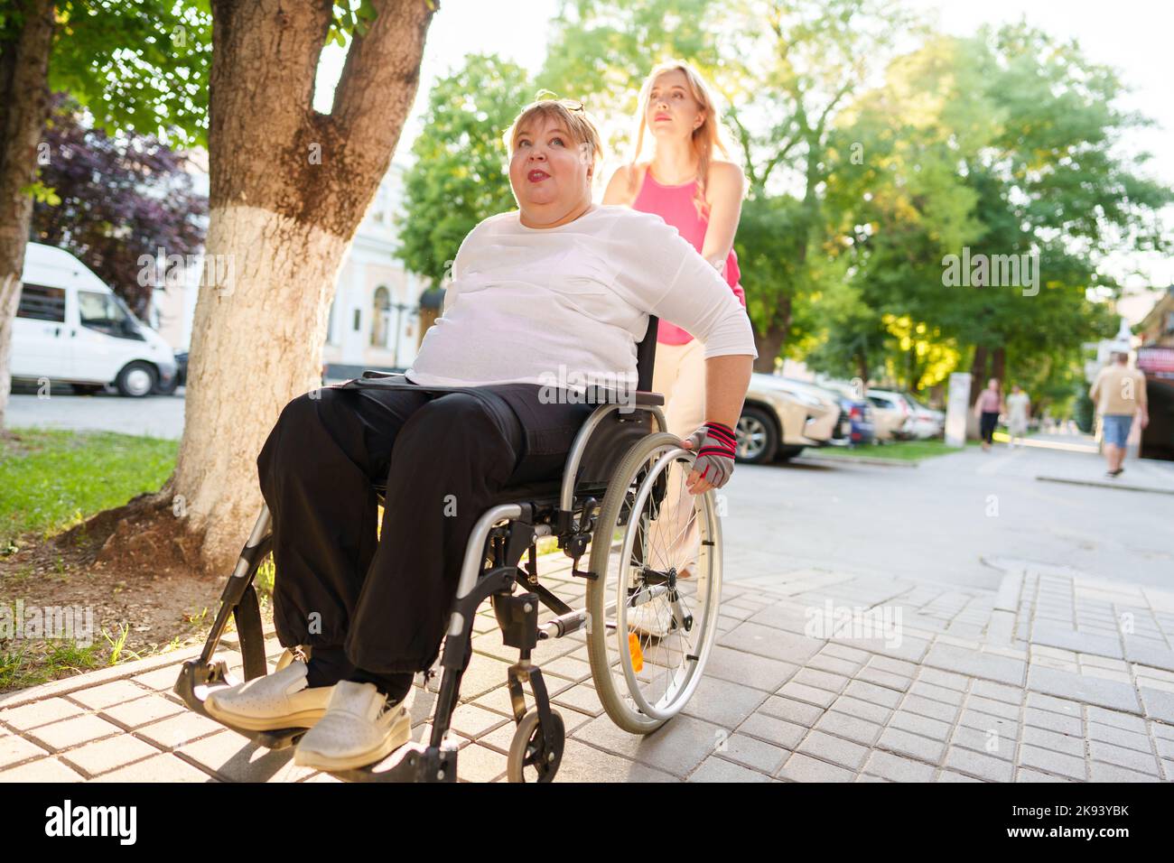 Young female caregiver pushing wheelchair with female person with ...