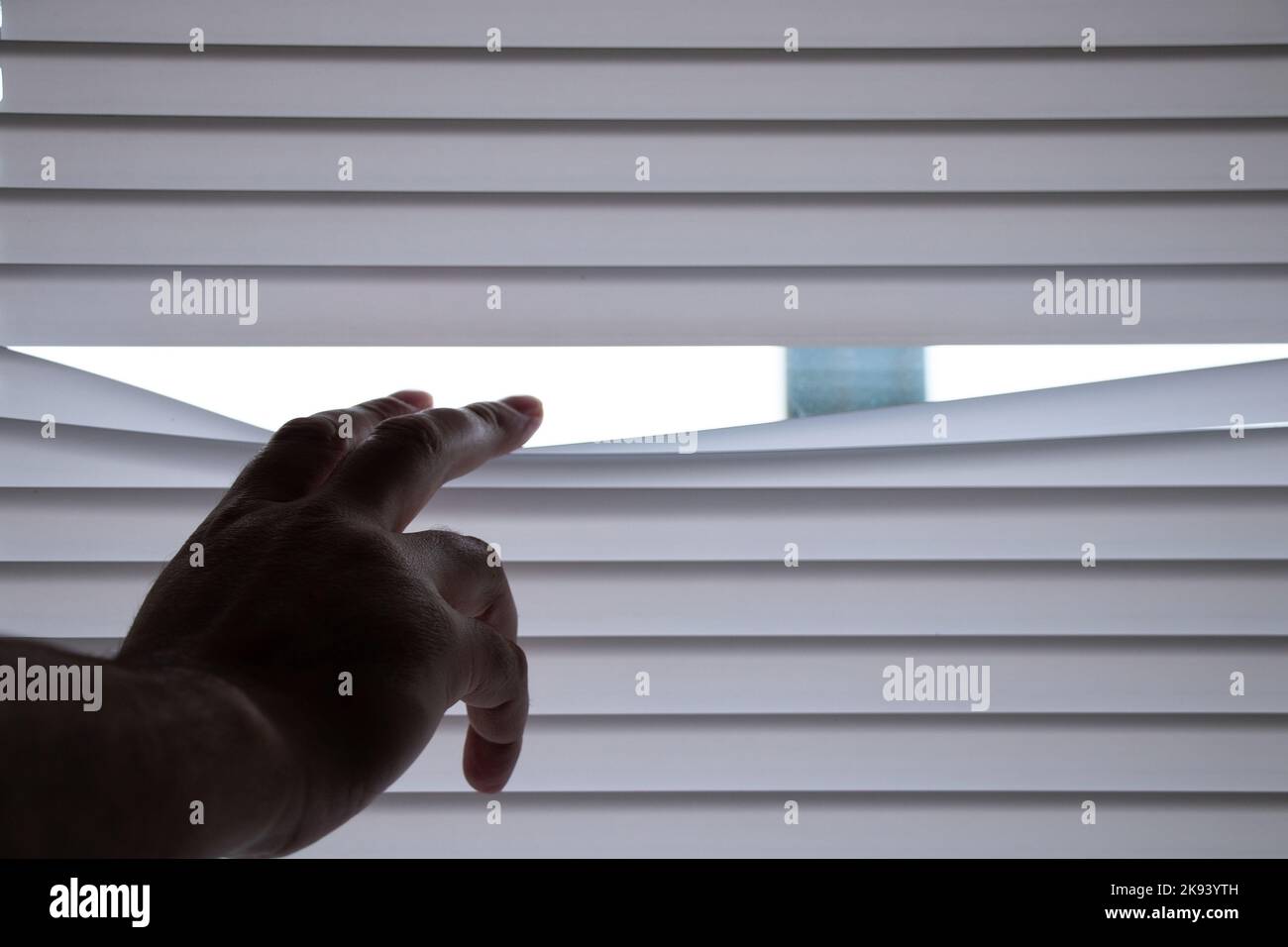 finger on the blinds on the window of the house, look out the window ...