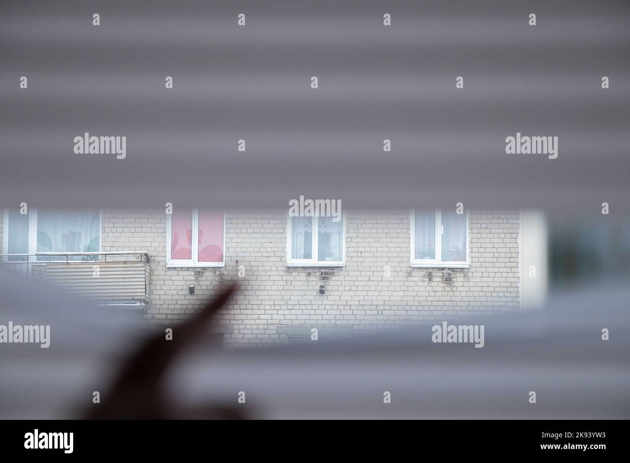 finger on the blinds on the window of the house, look out the window ...