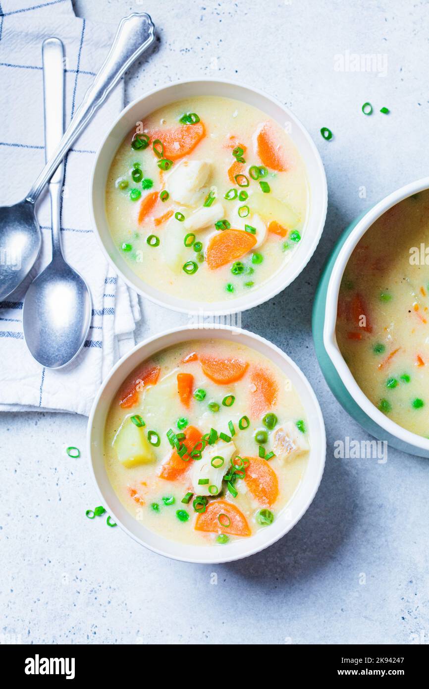 Fish cod chowder soup with green peas, potatoes and carrots in a white ...