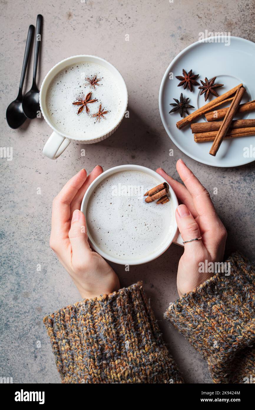 Homemade chai latte with cinnamon and star anise in white cup in hands ...