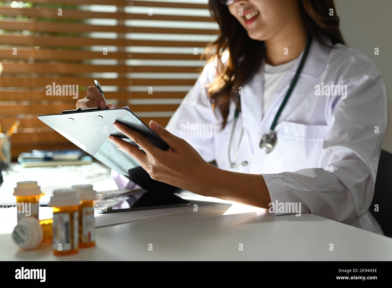 Smiling female doctor in white uniform taking writing medical journal ...