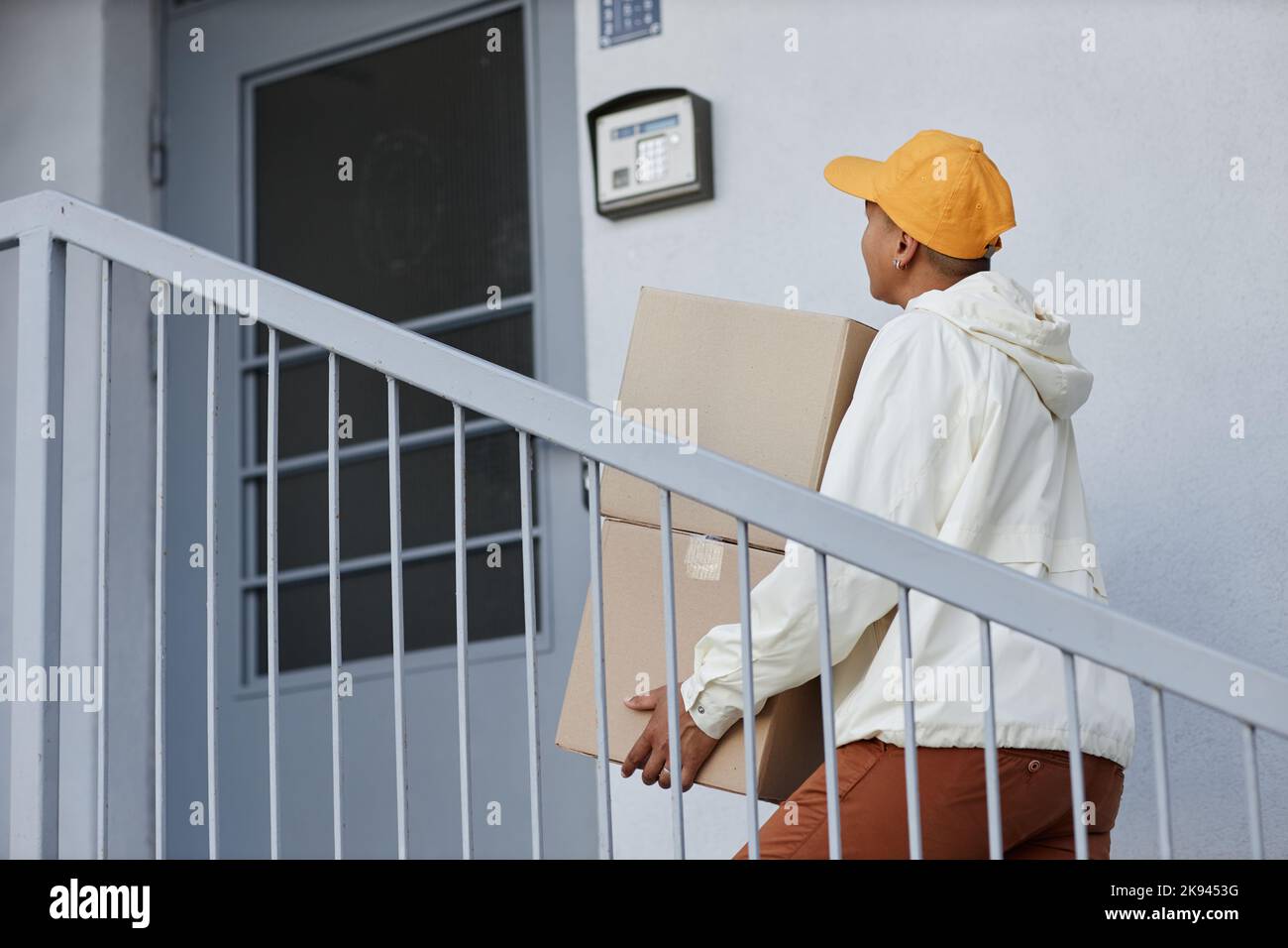 Back view of delivery worker going up stairs to house door with package ...