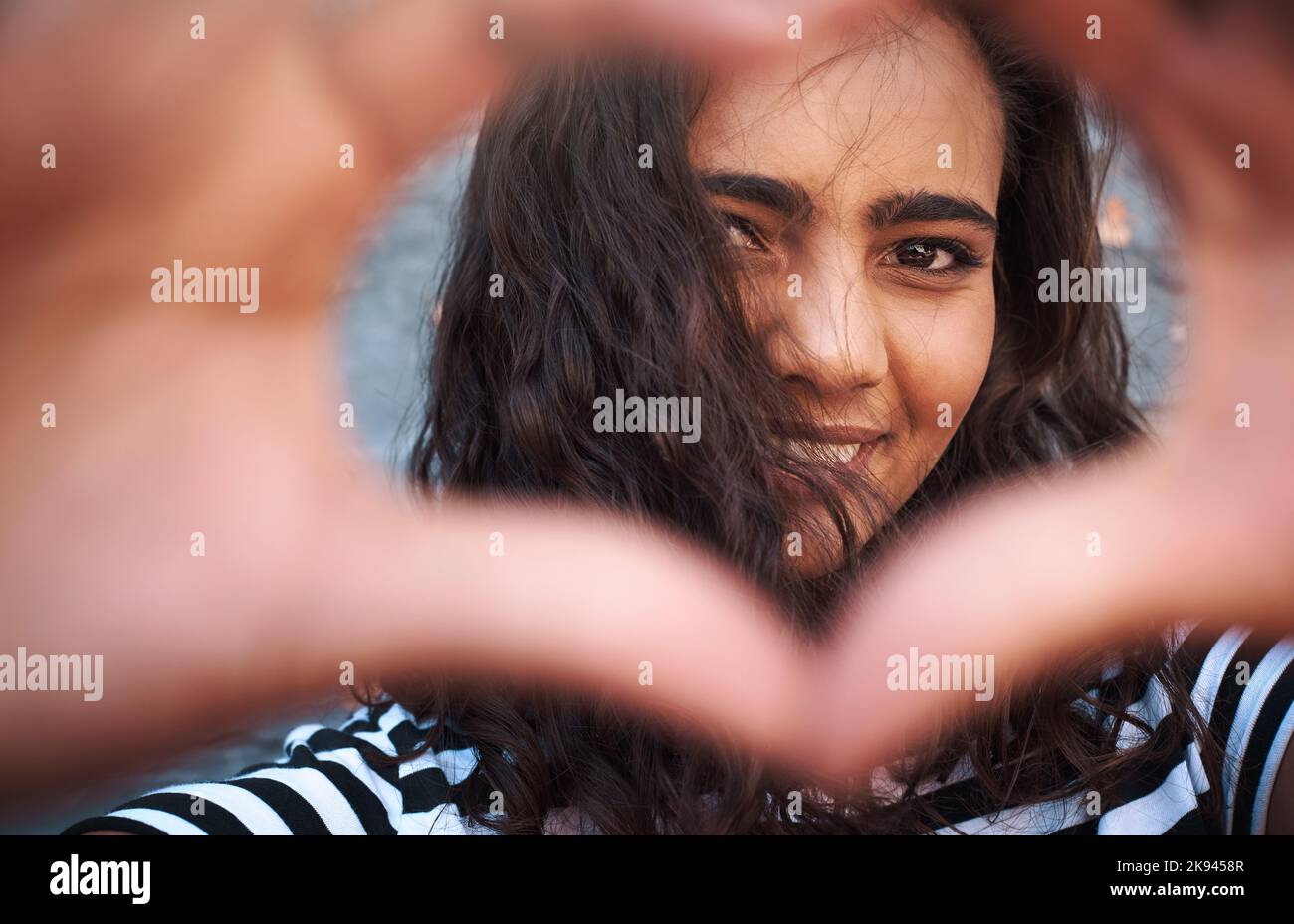Love surrounds us all. Portrait of a young woman making a heart shape ...