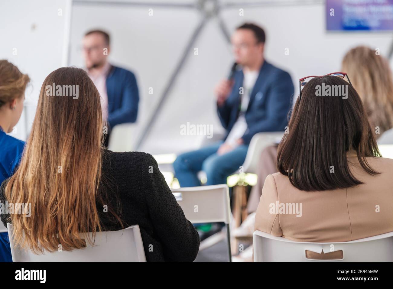 Anonymous businesswomen sitting on plastic chairs and listening to ...