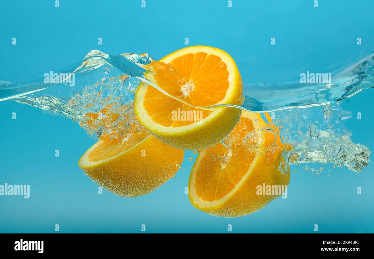 Fresh orange halves falling in water with splash on blue background ...