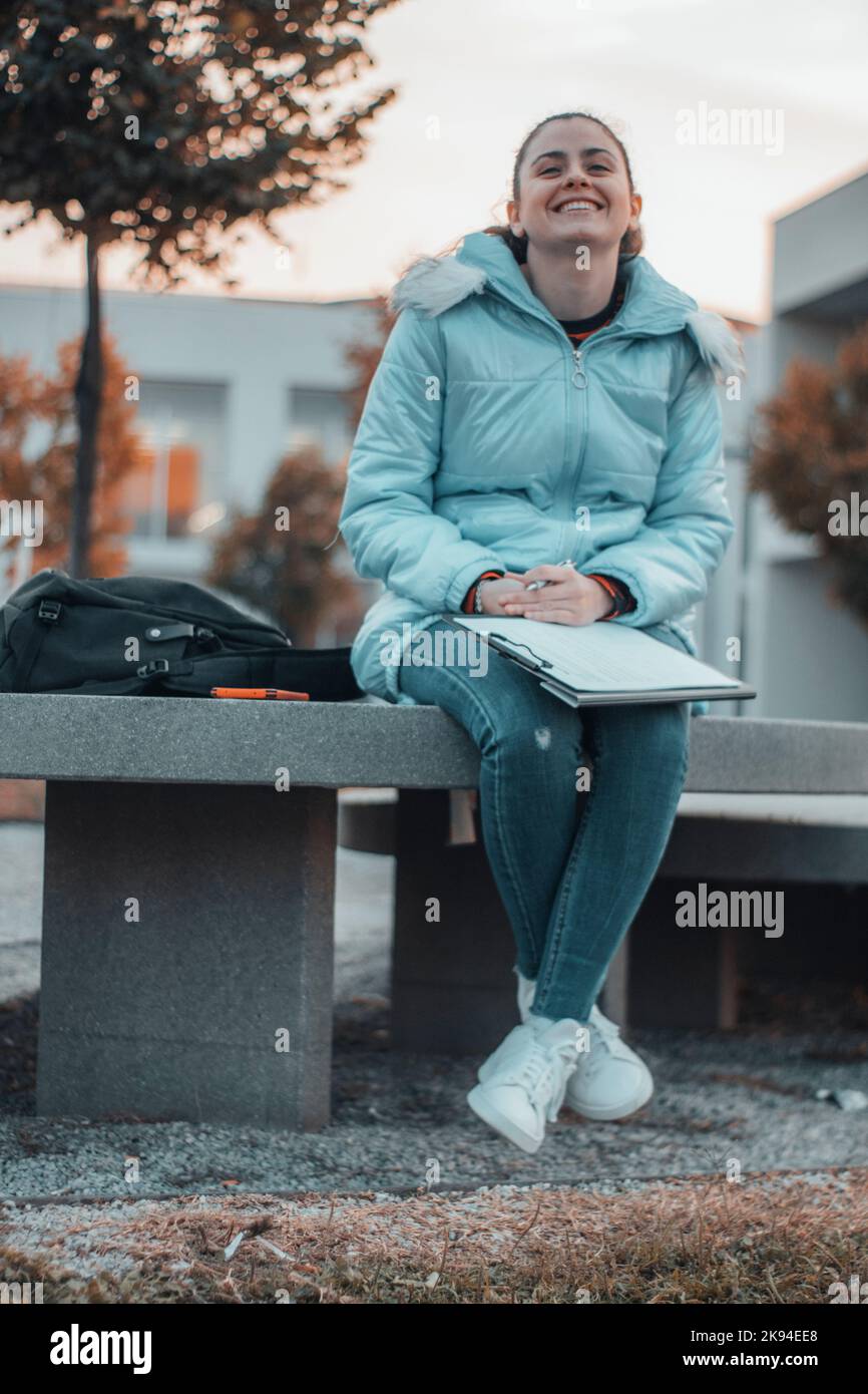 A smiling Spanish woman sitting on a bench against a school building ...