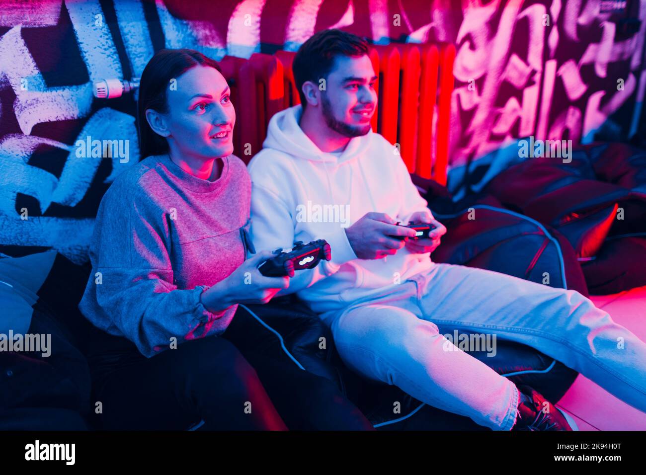Young man and woman couple plays on game console with gamepad sitting ...