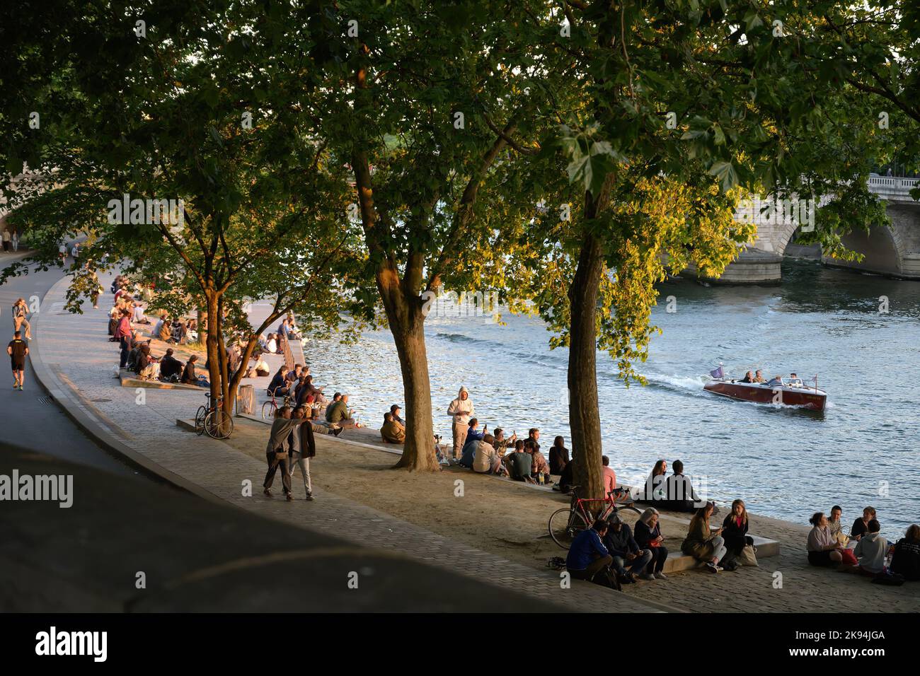 A crowd of people around the river during the golden hour in Paris ...