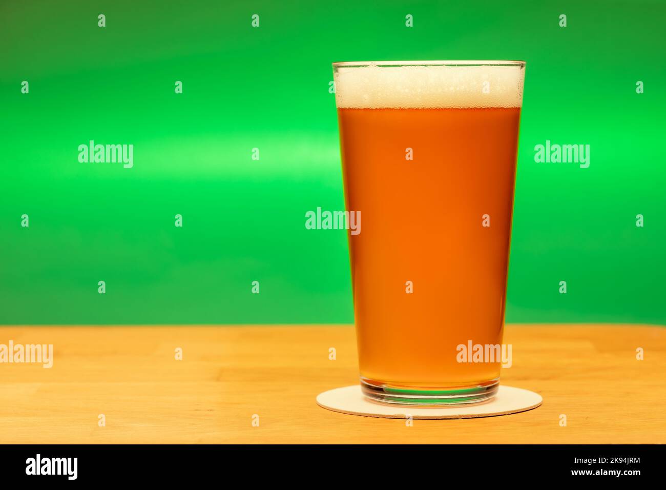 Full shaker pint glass of amber ale or beer on wooden table with green ...