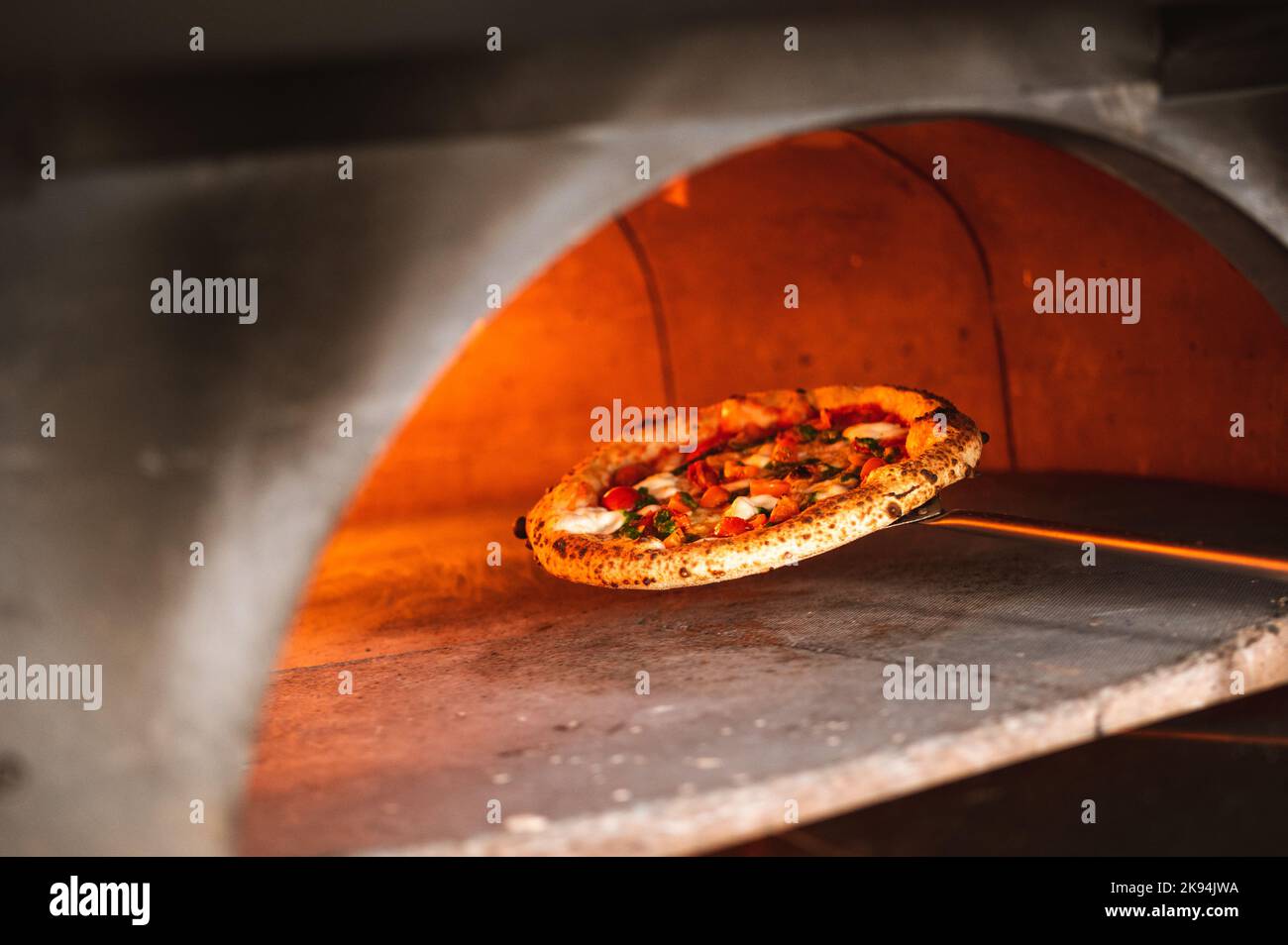 A closeup shot of pulling baked Neapolitan pizza out from an oven with ...