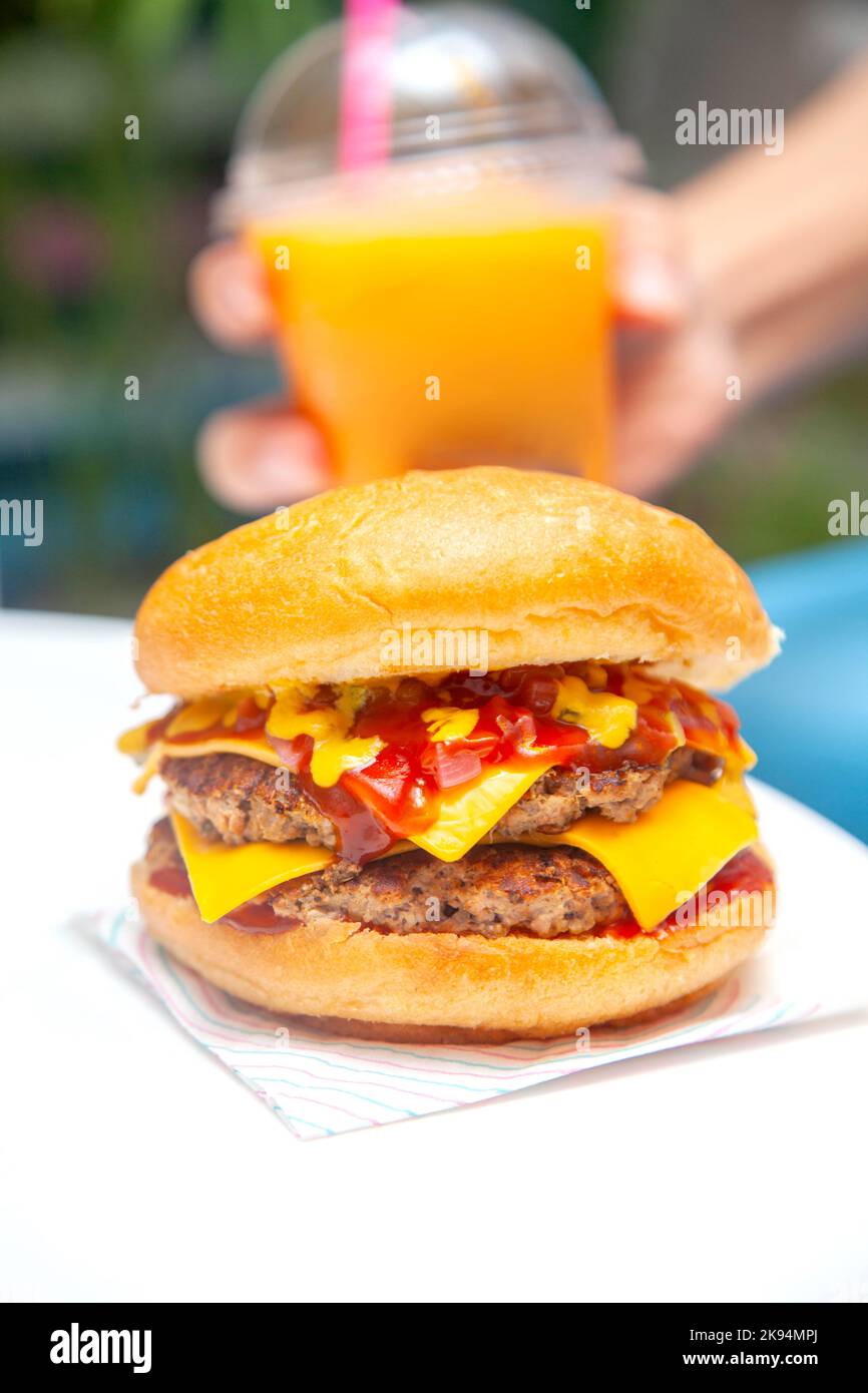 American cheeseburger with a hand holding orange cold drink juice Stock ...