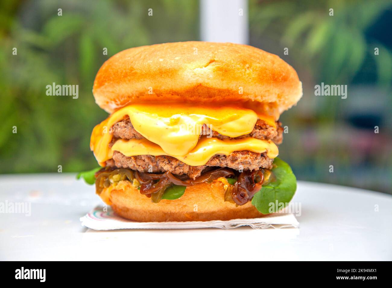 Queso double decker brioche burger in a cafe with lush green background ...