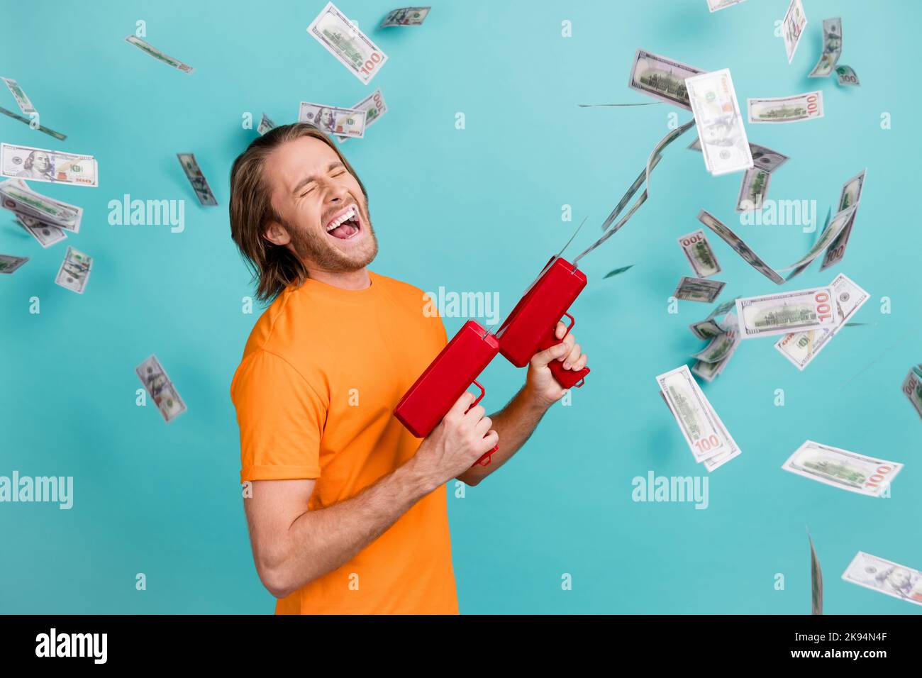 Photo of cool handsome man wear orange t-shirt shooting money gun money ...