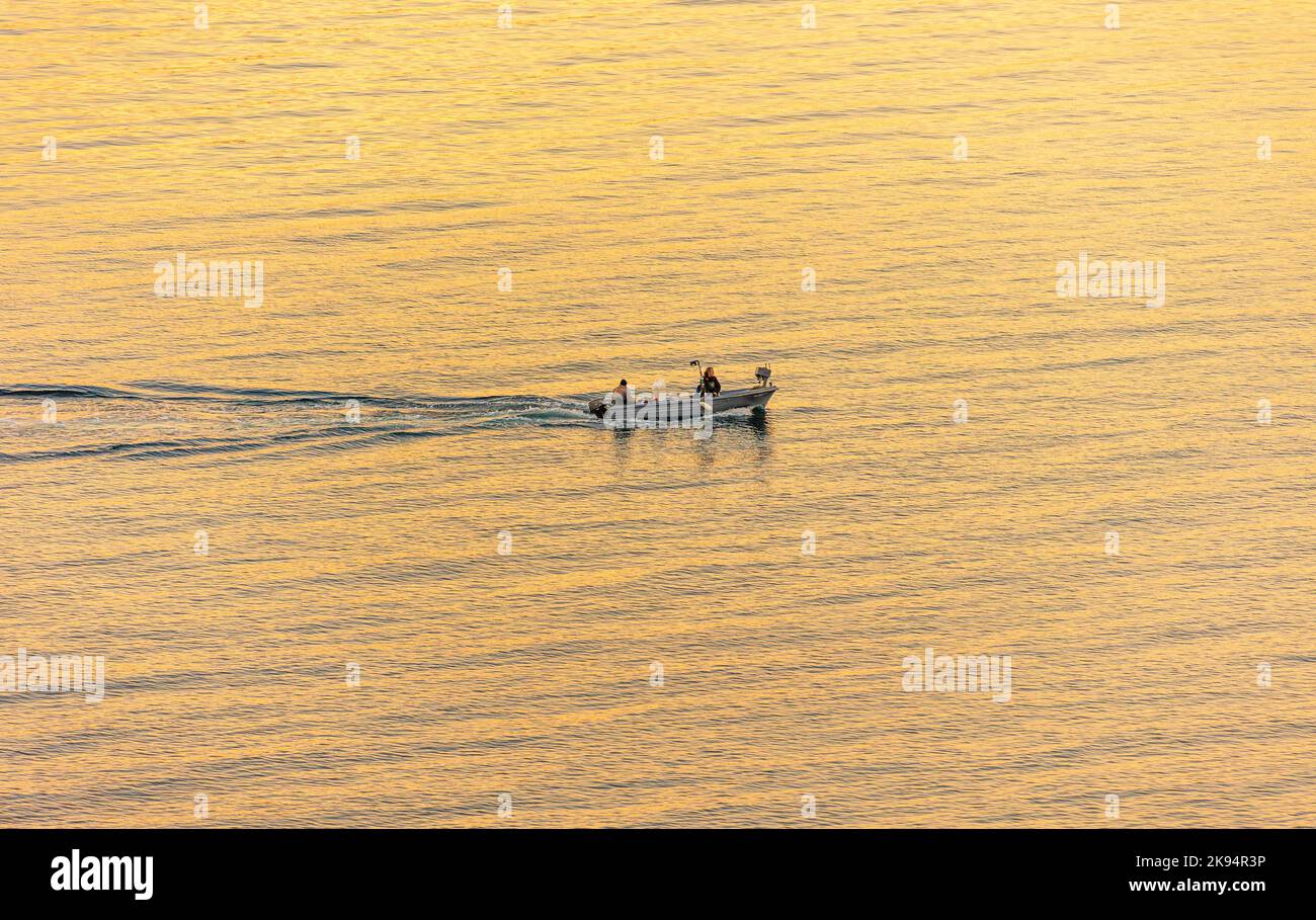 A boat with people driving on the sea water reflecting the soft orange ...
