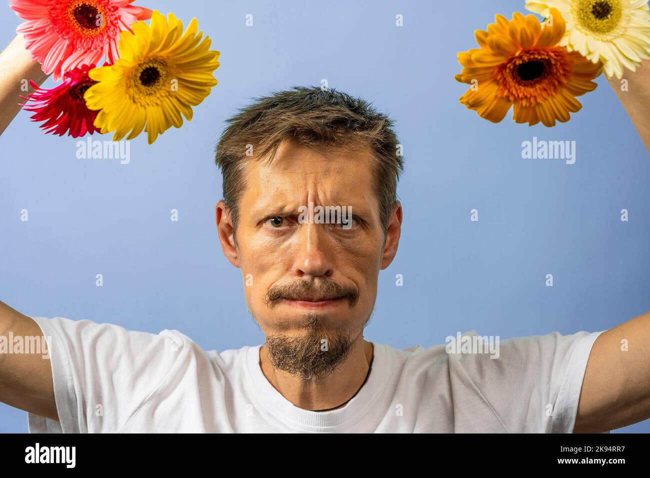 An angry, irritated man in a white T-shirt shakes and swings flowers ...