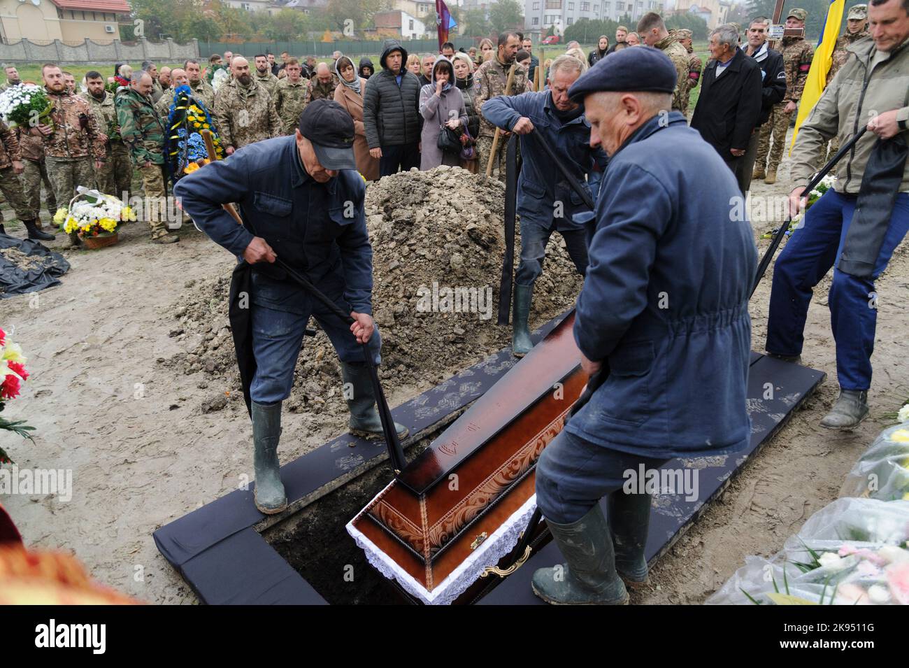 Lviv, Ukraine. 25th Oct, 2022. Men lower a coffin into a grave during ...