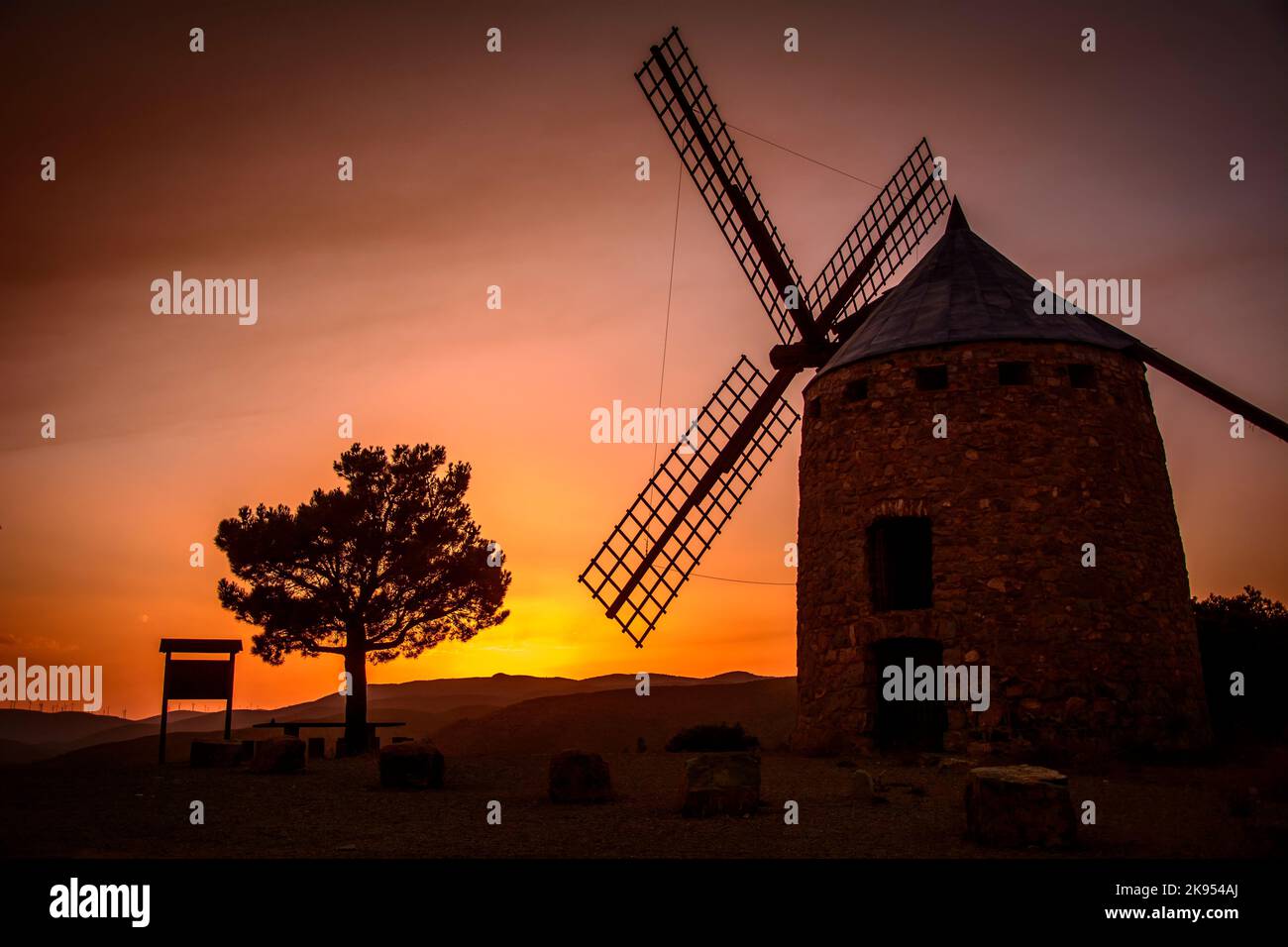 A historic stone windmill in the countryside during an orange sunset in ...
