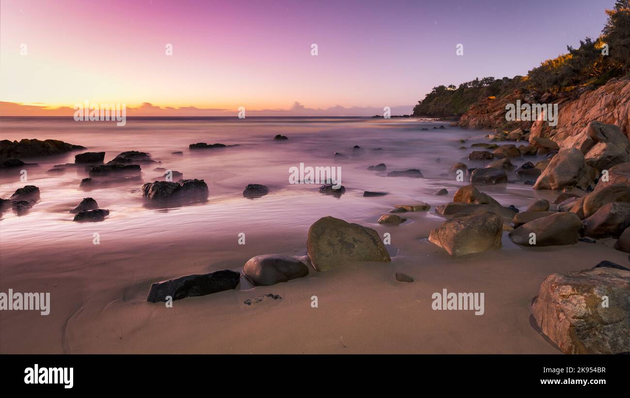 A scenic landscape of a calm rocky beach during colorful sunset Stock ...