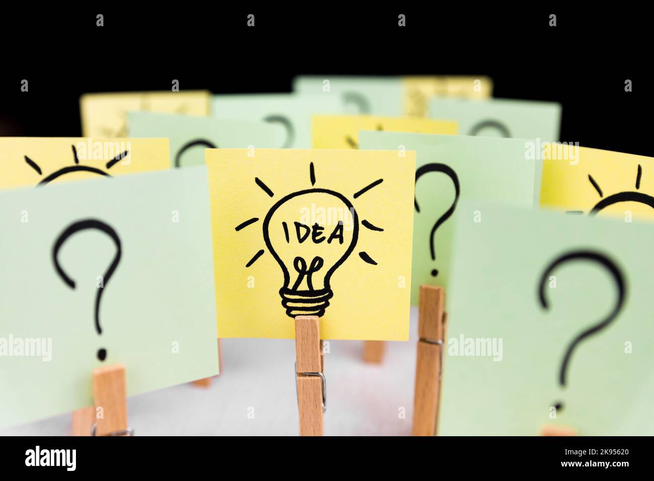 Light bulb doodle drawn on sticky note among many question marks. Hand ...