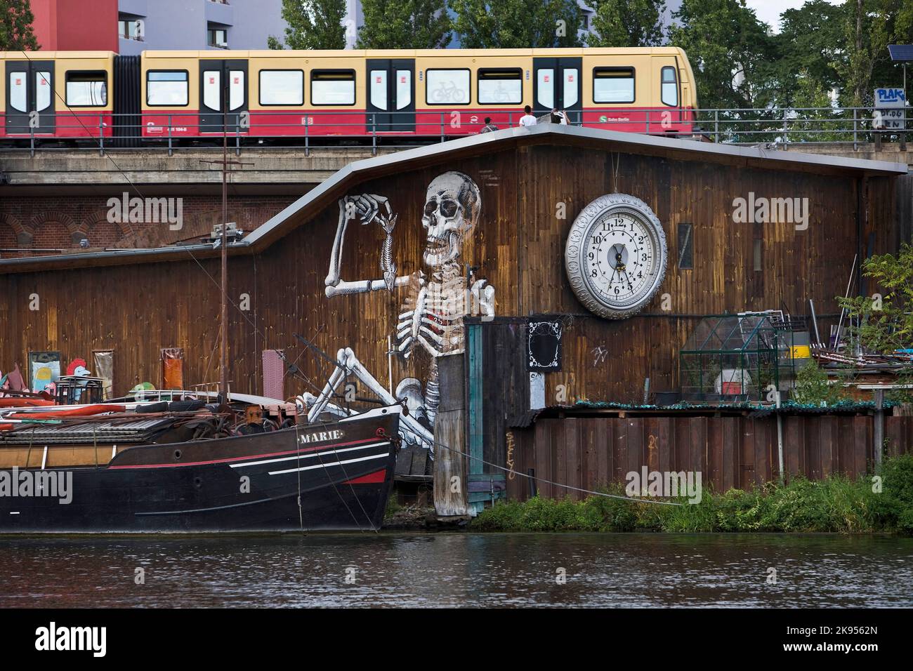 Wooden wall with clock and painted skeleton on the Spree with ship and ...