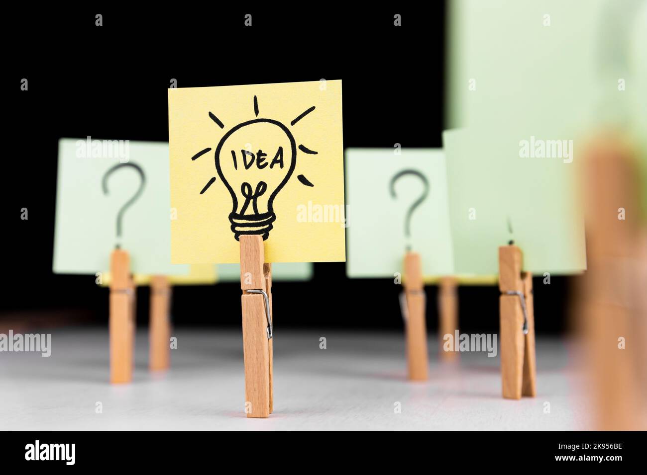 Light bulb doodle drawn on sticky note among many question marks. Hand ...