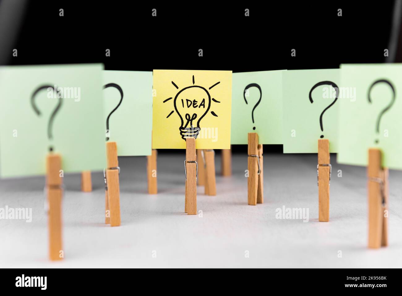 Light bulb doodle drawn on sticky note among many question marks. Hand ...