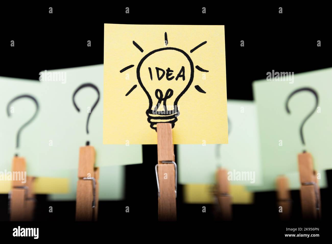 Light bulb doodle drawn on sticky note among many question marks. Hand ...